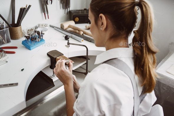 Focused on work. Side view of young female jeweler making a ring at her ...