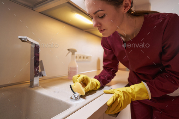 Concentrated serious professional janitor cleaning kitchen counter ...