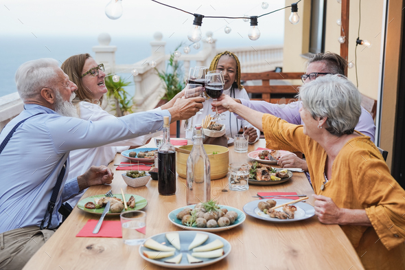 Elderly friends cheering at dinner on patio at home - Multiracial ...