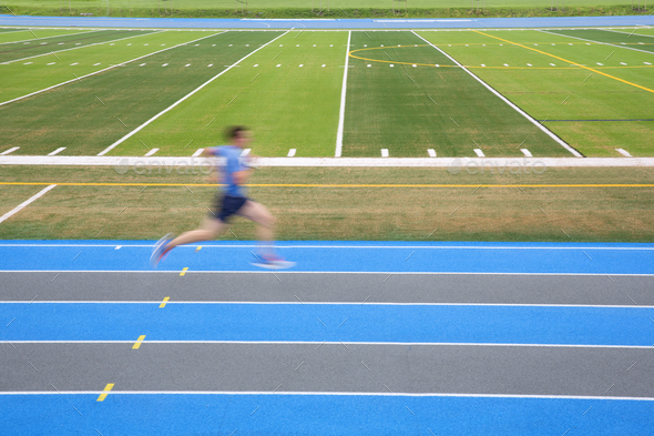 Side view of man running on blue track on sports field, motion blur ...