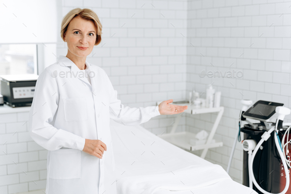 Portrait of charming beautician in white lab coat looking at camera ...