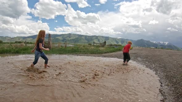 Slow motion of kids paying in mud puddle and kicking water on each ...