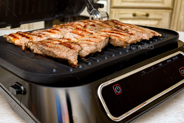 The process of cooking pork meat on electric grill close-up Stock Photo ...