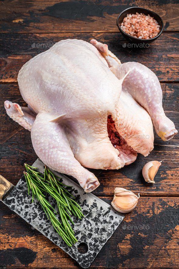Whole chicken, raw poultry on a butchery table with meat cleaver. Dark ...