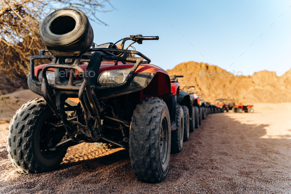 Close-up view from below of an ATV in the desert. A column of ATVs ...