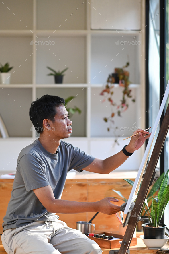 Side view of young asian man painting on canvas in art studio. Stock ...