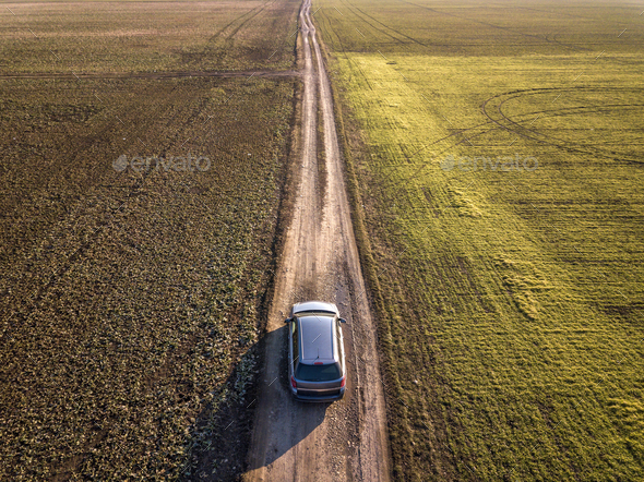Aerial view of car driving by straight ground road through green fields ...