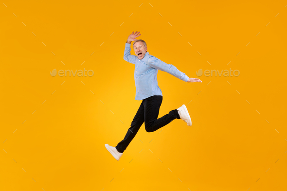 Excited mature man jumping up at orange studio Stock Photo by Prostock ...
