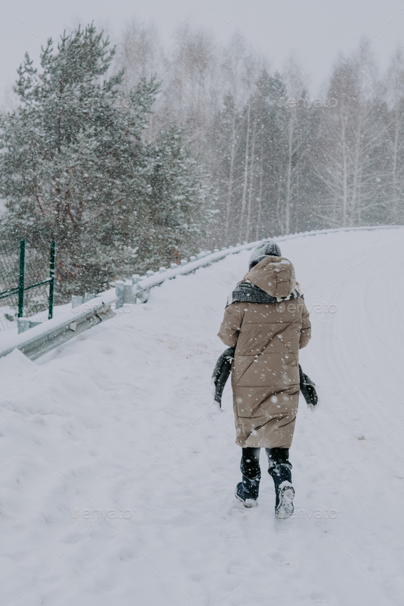 A woman walks in a field near the forest, in a very strong blizzard ...