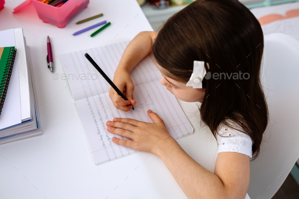 Girl doing homework sitting at a desk Stock Photo by davidpereiras