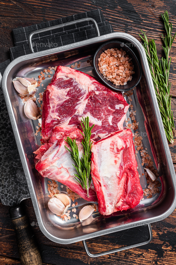 Raw beef Short Ribs in steel tray with rosemary. Wooden background. Top ...