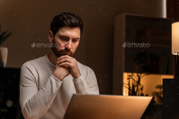 Young tired man sitting at the workplace with laptop and looking at the ...