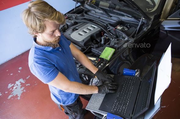 Mechanic using a computer while fixing a car Stock Photo by westend61