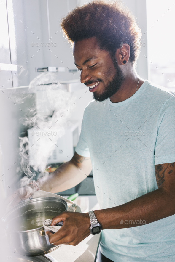 Smiling man holding cooking pot with hot water Stock Photo by westend61
