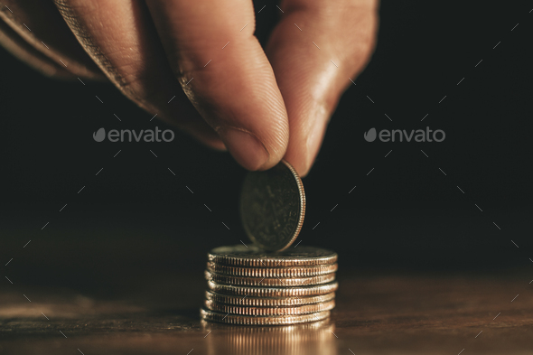 Hand holding coin on top of stack of coins Stock Photo by westend61