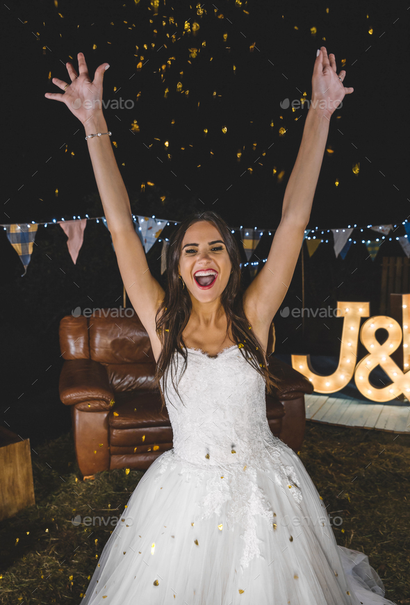 Cheerful bride raising her arms while confetti falling over her on a ...