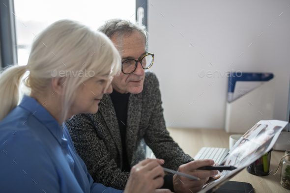 Two senior colleagues working together at desk in office examining ...