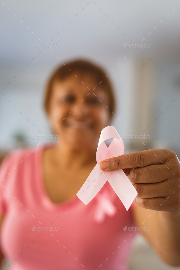 Smiling senior woman showing pink ribbon representing breast cancer ...