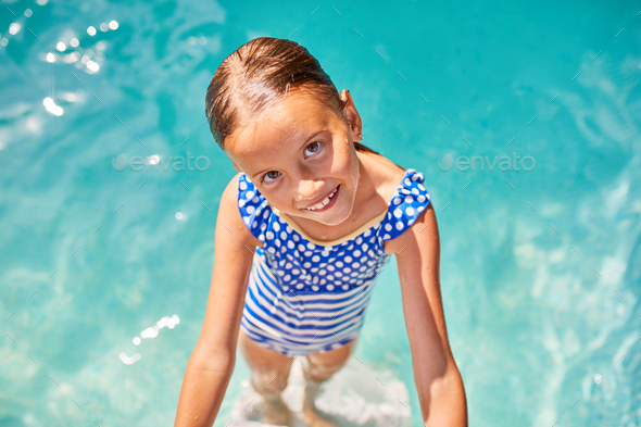 A child on the steps climbing out of the pool, little girl having fun ...