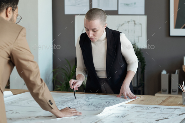 Confident businesswoman bending over table with blueprint Stock Photo ...
