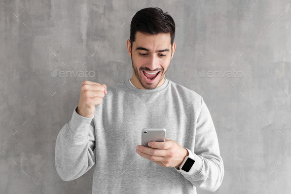 Young man clenching fist and celebrating while holding mobile phone in ...