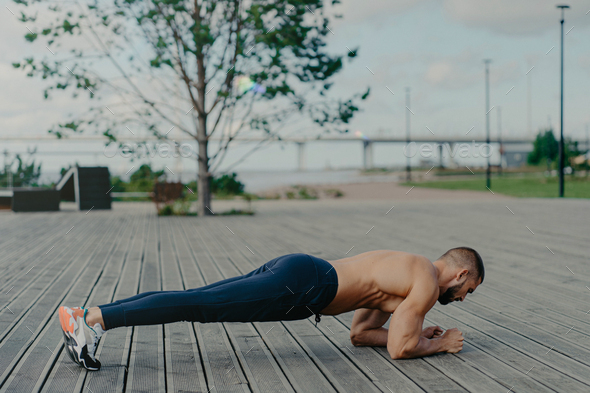 Sporty man stands in plank pose, practices yoga outdoor and dressed in ...