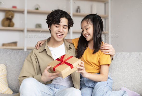 Smiling happy chinese young guy receives gift from teenager daughter in ...