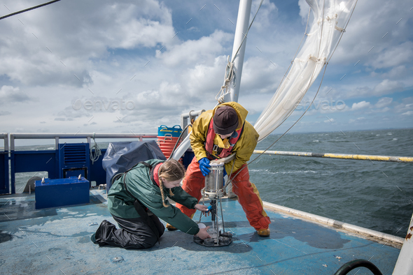 Marine biologist taking plankton samples from net on research ship ...