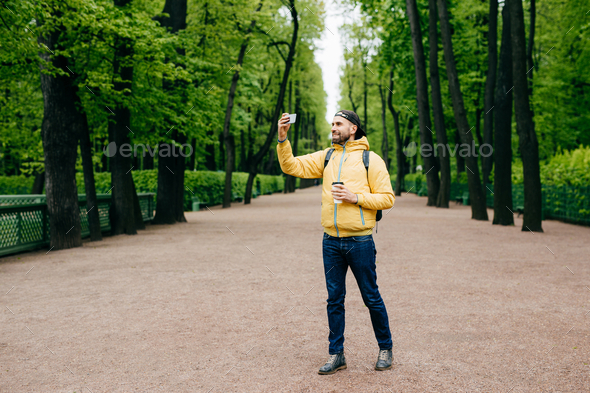 Bearded young man dressed in yellow jacket, jeans and black cap having ...