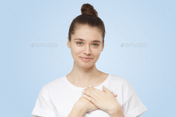 Smiling beautiful young woman keeps hands on chest, expresses deep ...