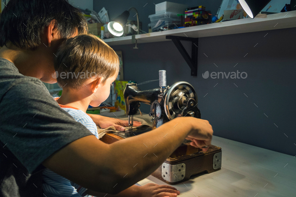 Over shoulder view of boy with father learning to turn sewing machine ...