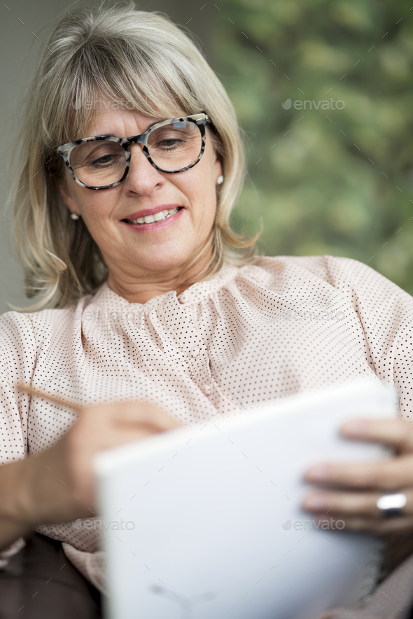Smiling mature woman drawing on sketchbook Stock Photo by westend61