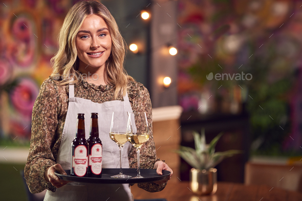 Portrait Of Smiling Female Server Holding Tray Of Drinks In Cool Bar Or ...