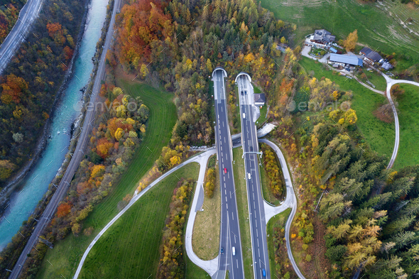 Top dawn aerial view of freeway speed road going out from undeground tunnel between yellow ...