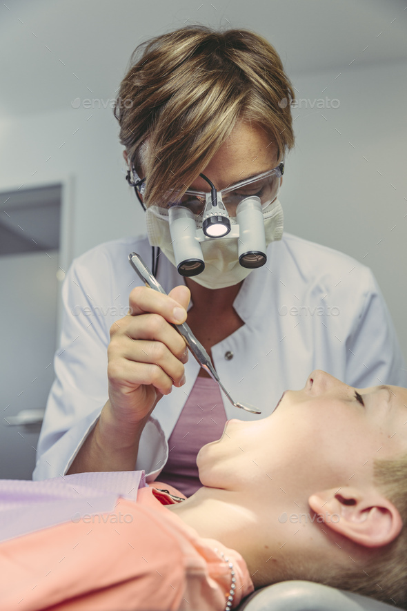 Denist examining boy's teeth, using head magnifiers and dental ...