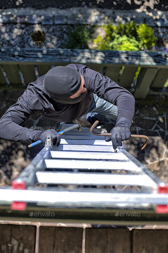 Burglar with crowbar climbing up ladder at house wall Stock Photo by ...
