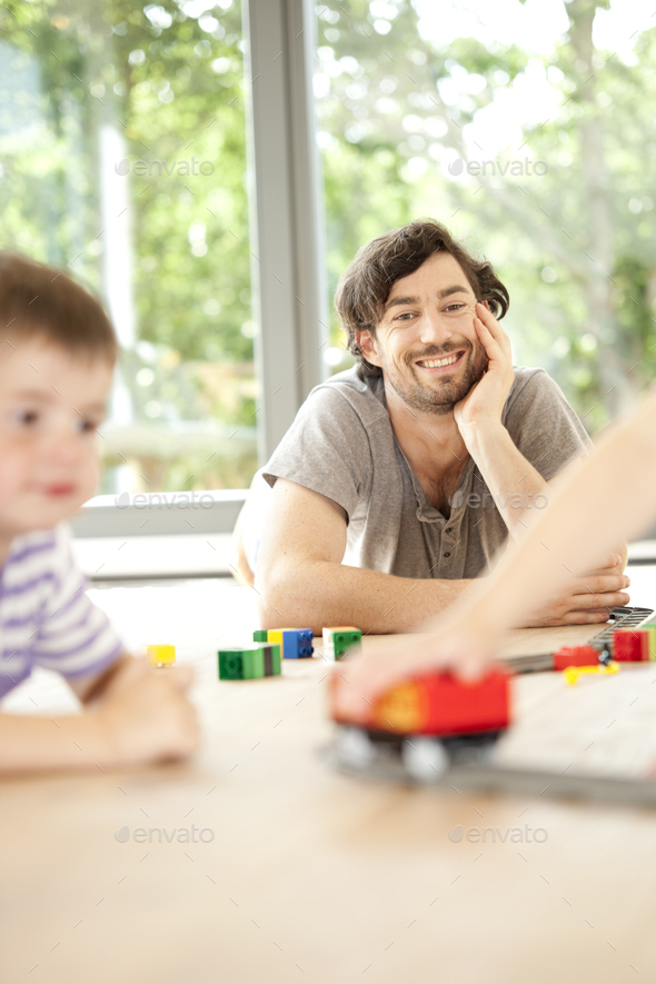 Father lying on floor watching children playing with toy train Stock ...