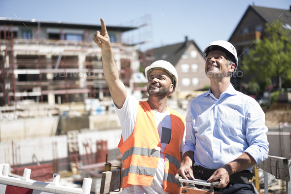 Smiling construction worker talking to man on construction site Stock ...