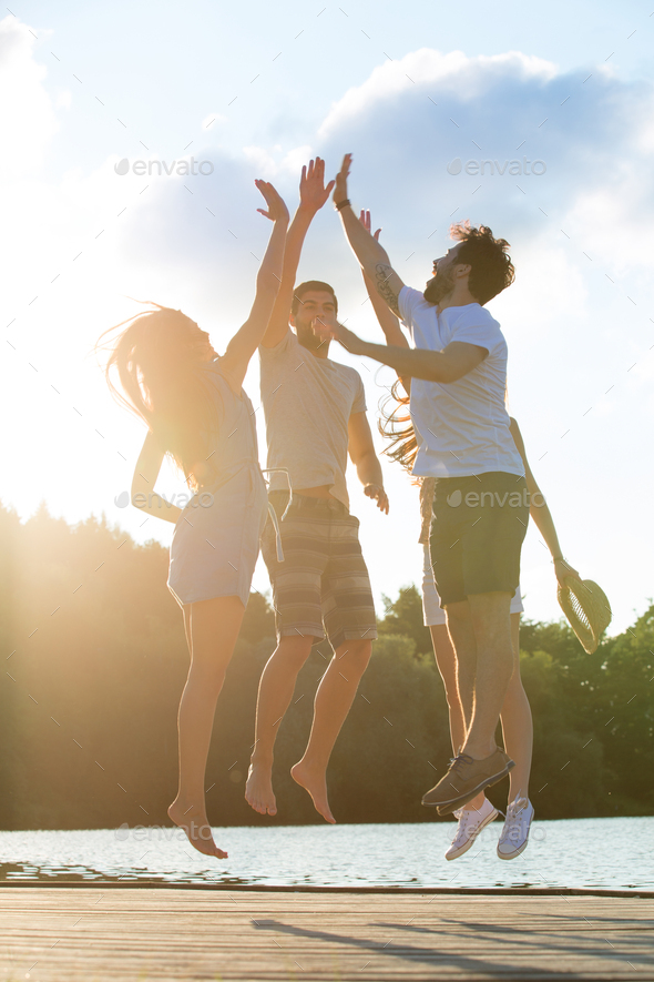 Four friends high fiving at a lake in backlight Stock Photo by westend61