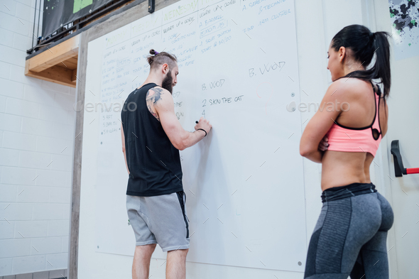 Young man personal trainer indoor gym writing on whiteboard planning ...