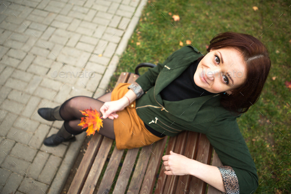 A woman with a bob haircut and a yellow fallen maple leaf in a green ...