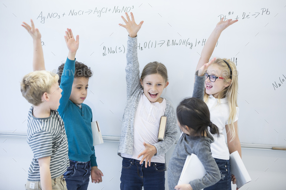Happy pupils raising their hands at whiteboard with formulas in class ...