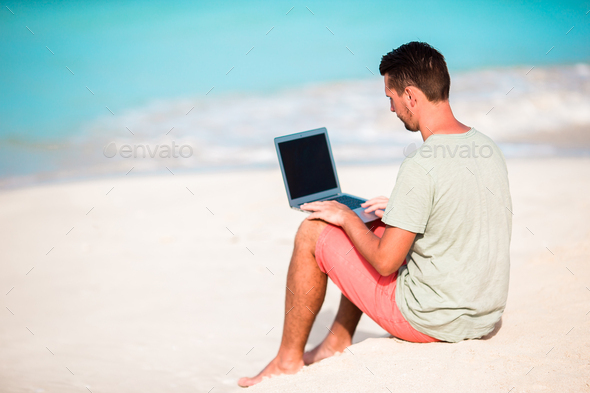 Young man sitting on sand with laptop on tropical caribbean beach. Man ...