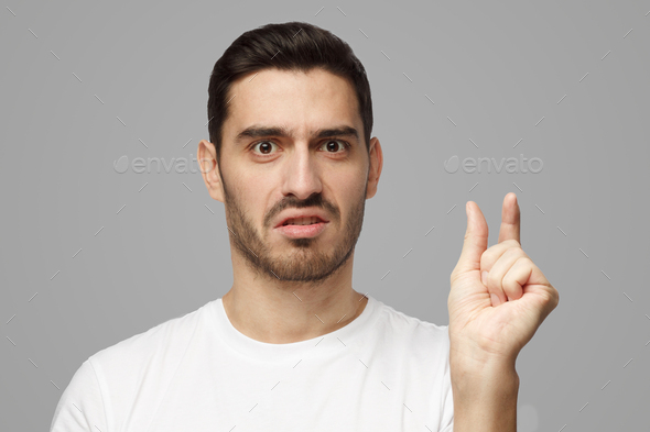 Young man gesticulates with hands, showing little size with unpleased ...