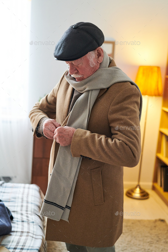 Senior man buttoning his coat while getting dressed before going out ...