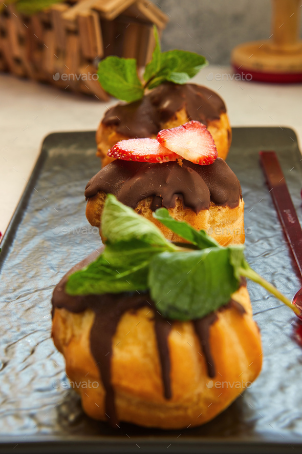 Stack eclair of profiteroles with dark melted chocolate on a black dish ...