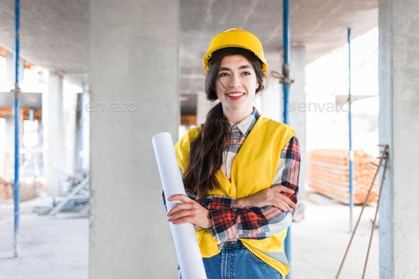 Confident girl engineer builder stands at a construction site holding ...