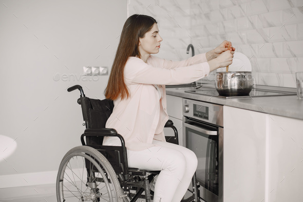 Disabled Young Woman Cooking In Her Kitchen Stock Photo by prostooleh