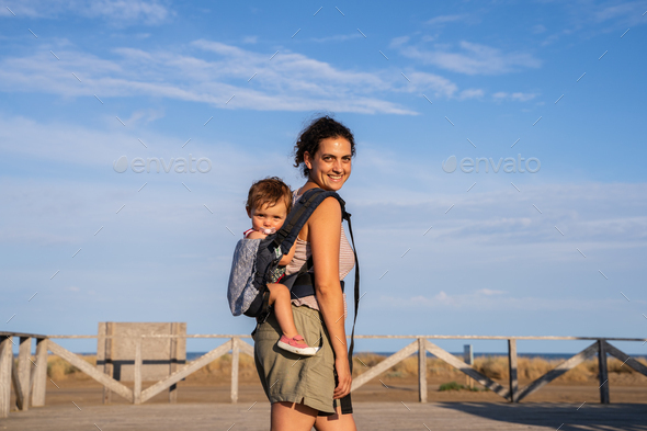 Profile of a mother carrying a baby on her back in a baby carrier next ...