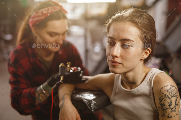 Beautiful lady sitting in tattoo salon while tattoo artist drawing ...